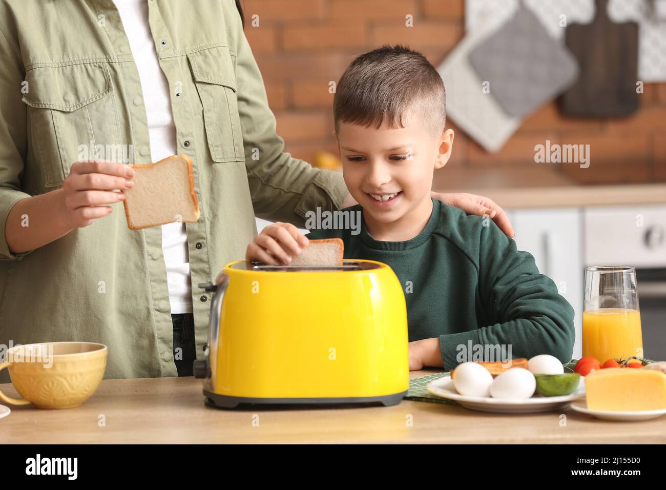 Little boy and his mother putting bread slices into toaster in kitchen ...