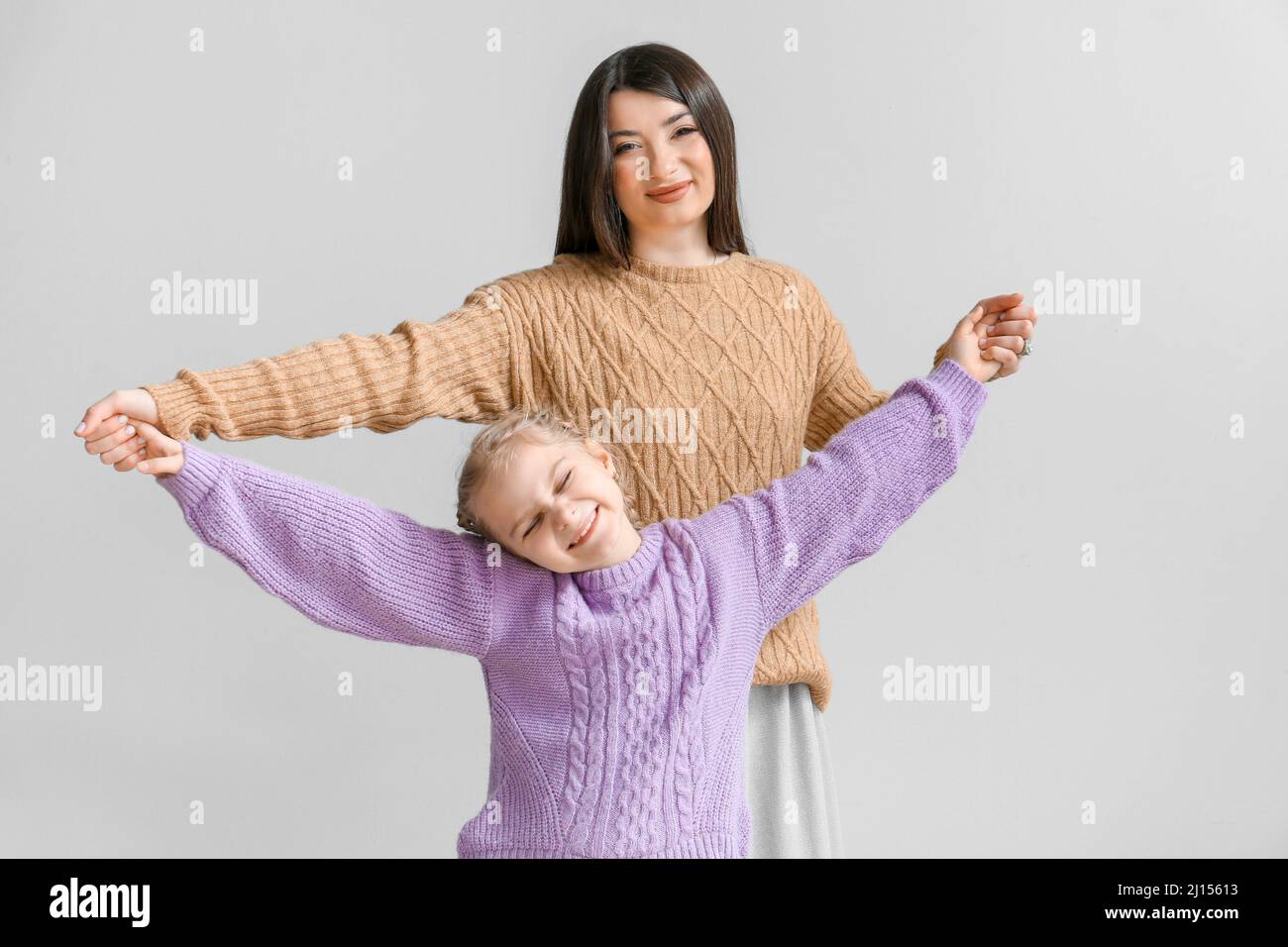 Little girl and her mother in warm sweaters holding hands on light ...