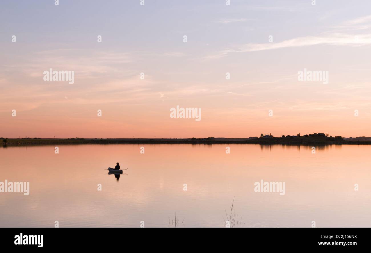 Fisherman floating on the still lake during sunset Stock Photo - Alamy