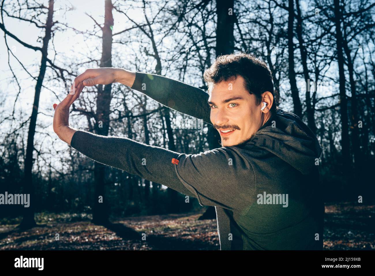 Runner is doing stretching in the woods. Young man with blue eyes and ...