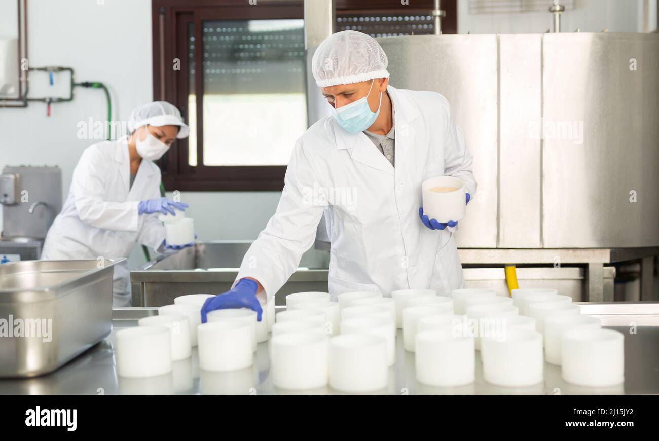 Cheesemaker in protective mask working in shaping workshop of cheese ...