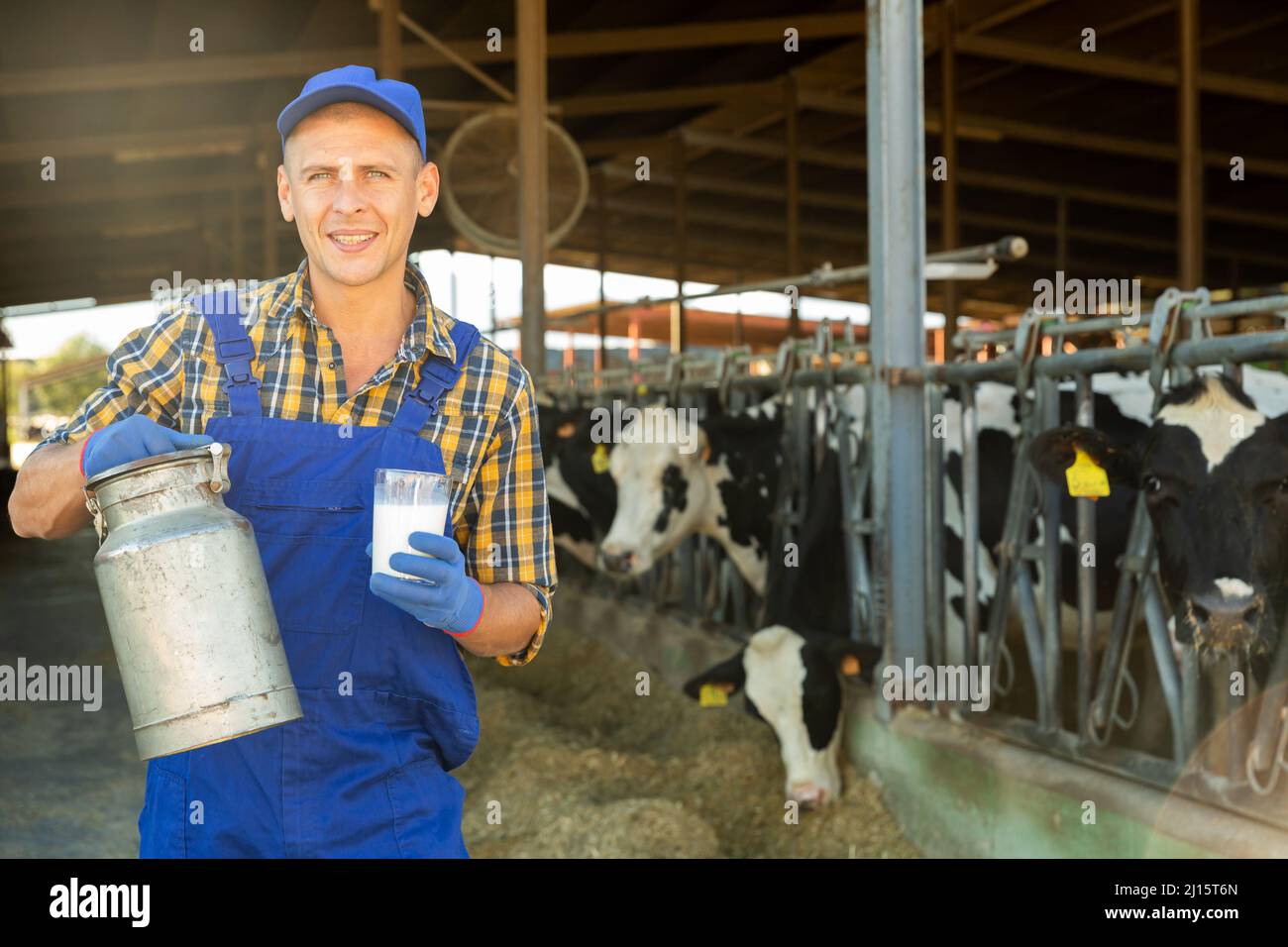 Portrait of positive dairy farm worker in blue overalls with can of ...