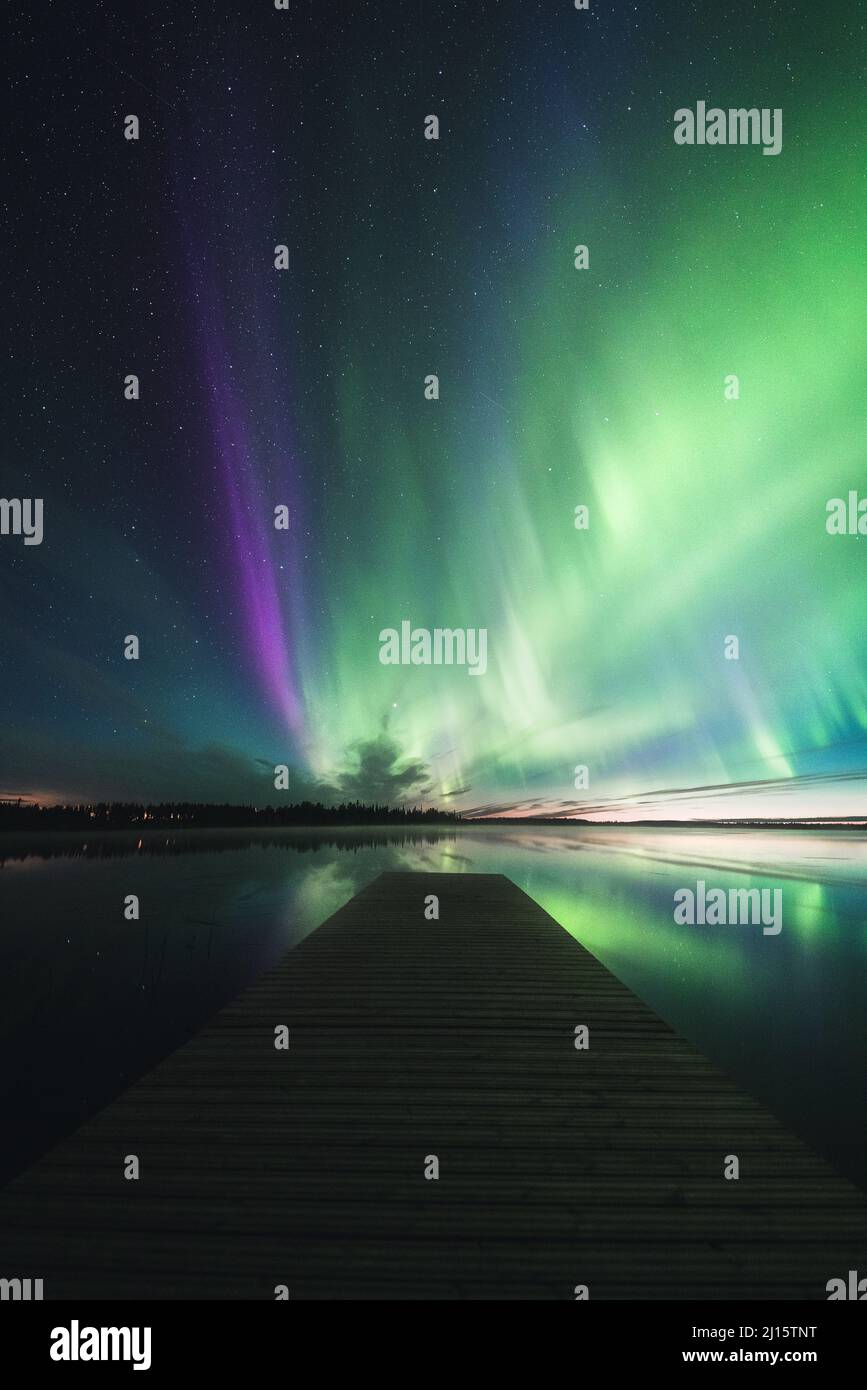 A vertical shot of a wooden dock under a beautiful Aurora Borealis ...
