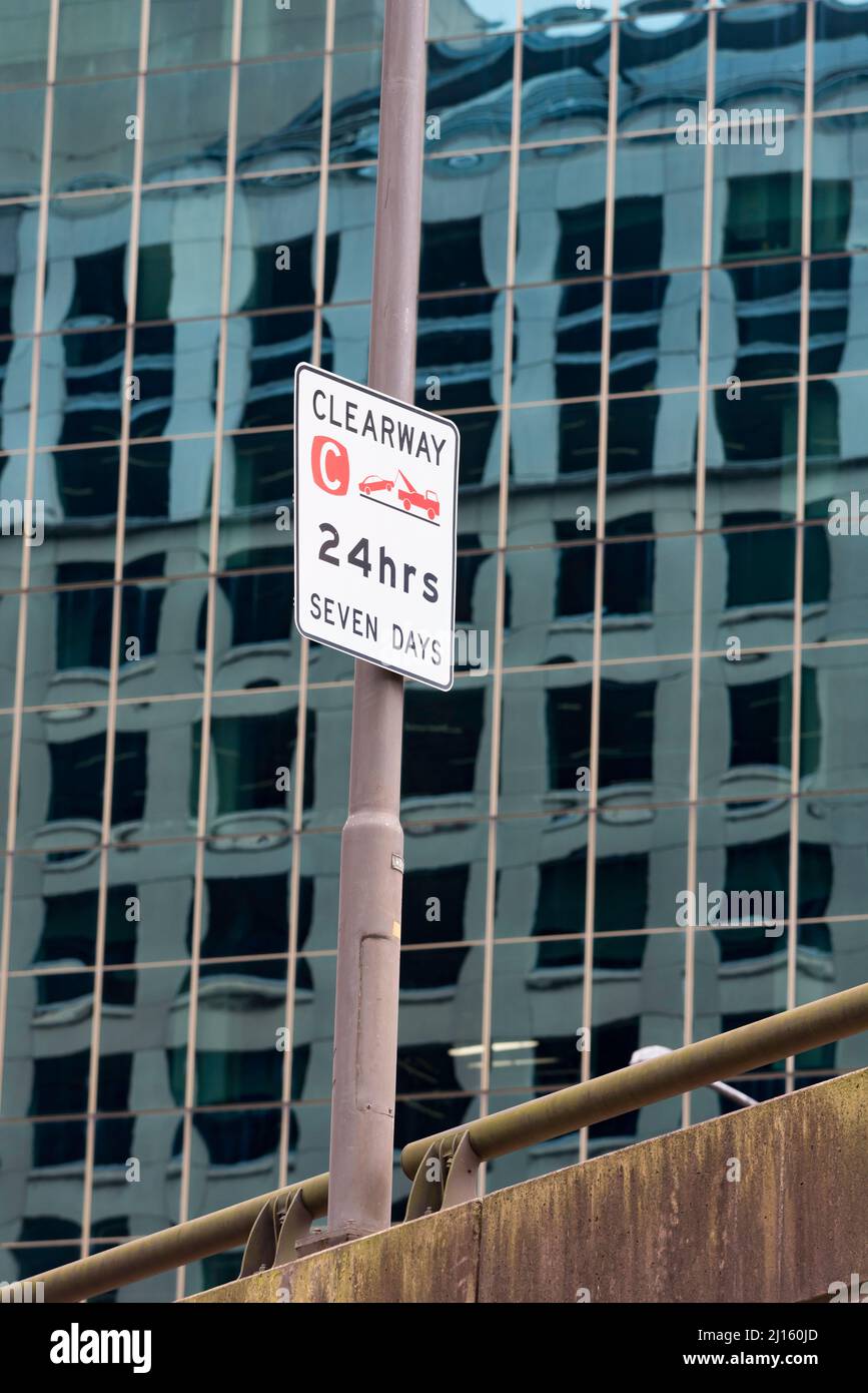A 24hr clearway traffic sign in front of a glass curtain wall building ...