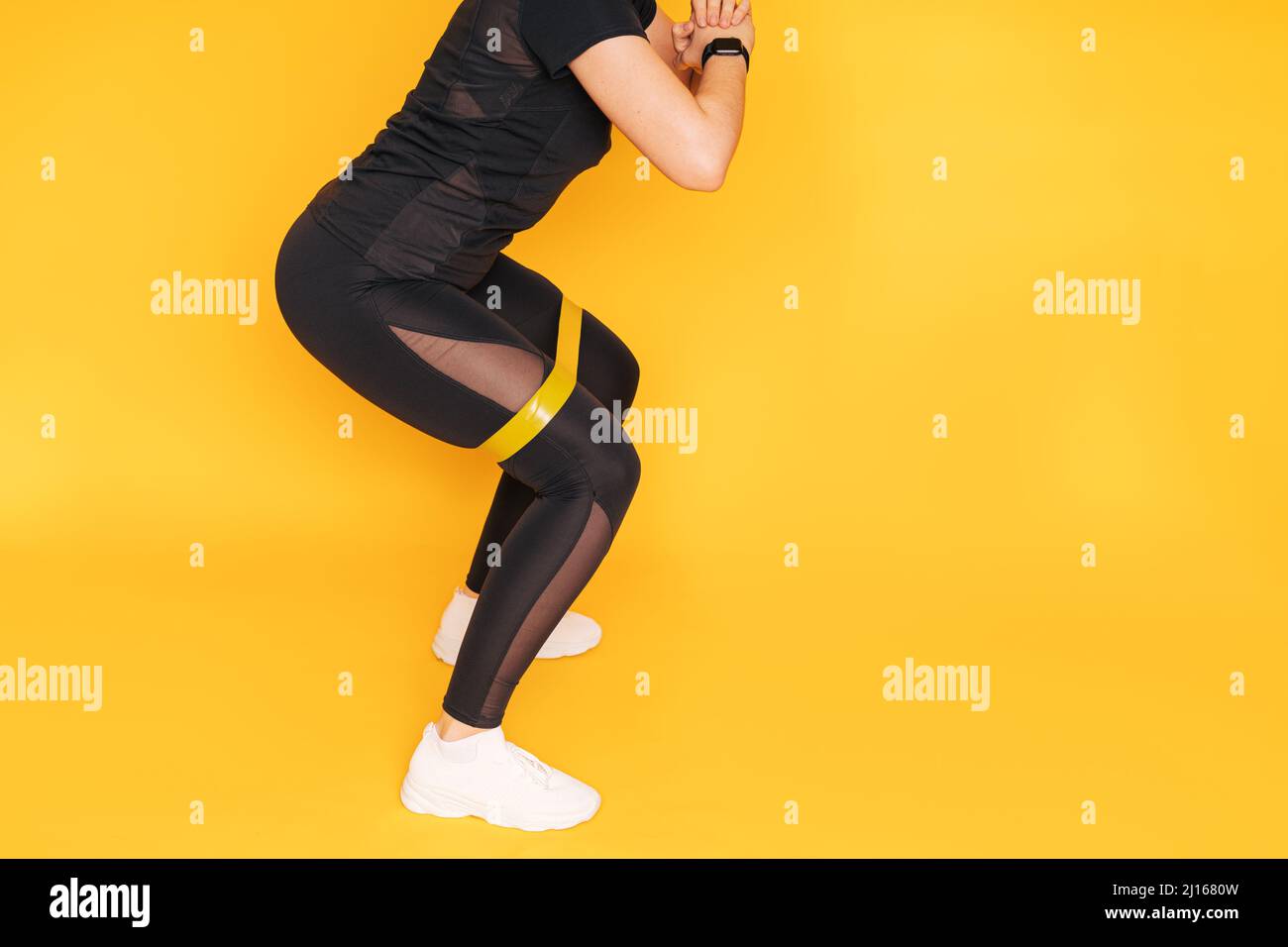 Girl crouches with an elastic band on her legs against yellow ...