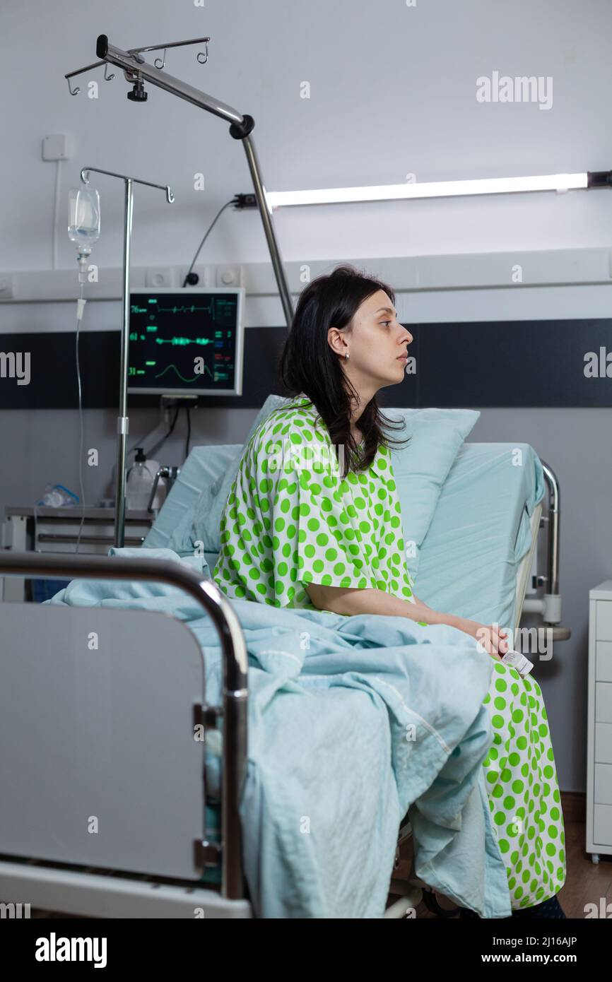 Bored woman recieving iv drip line treatment sitting on bedside looking ...