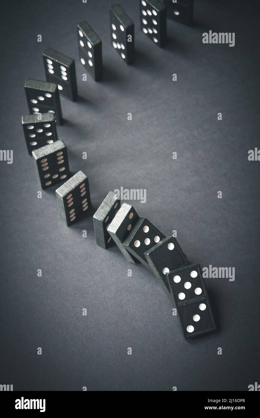 Black dominoes chain on a dark table background. Domino effect concept ...