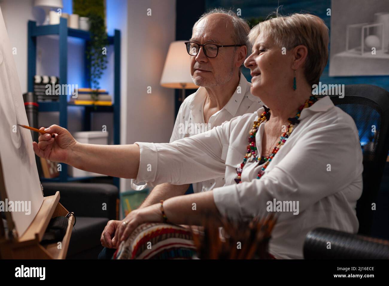 Older woman art teacher explaining freehand technique to elderly man ...