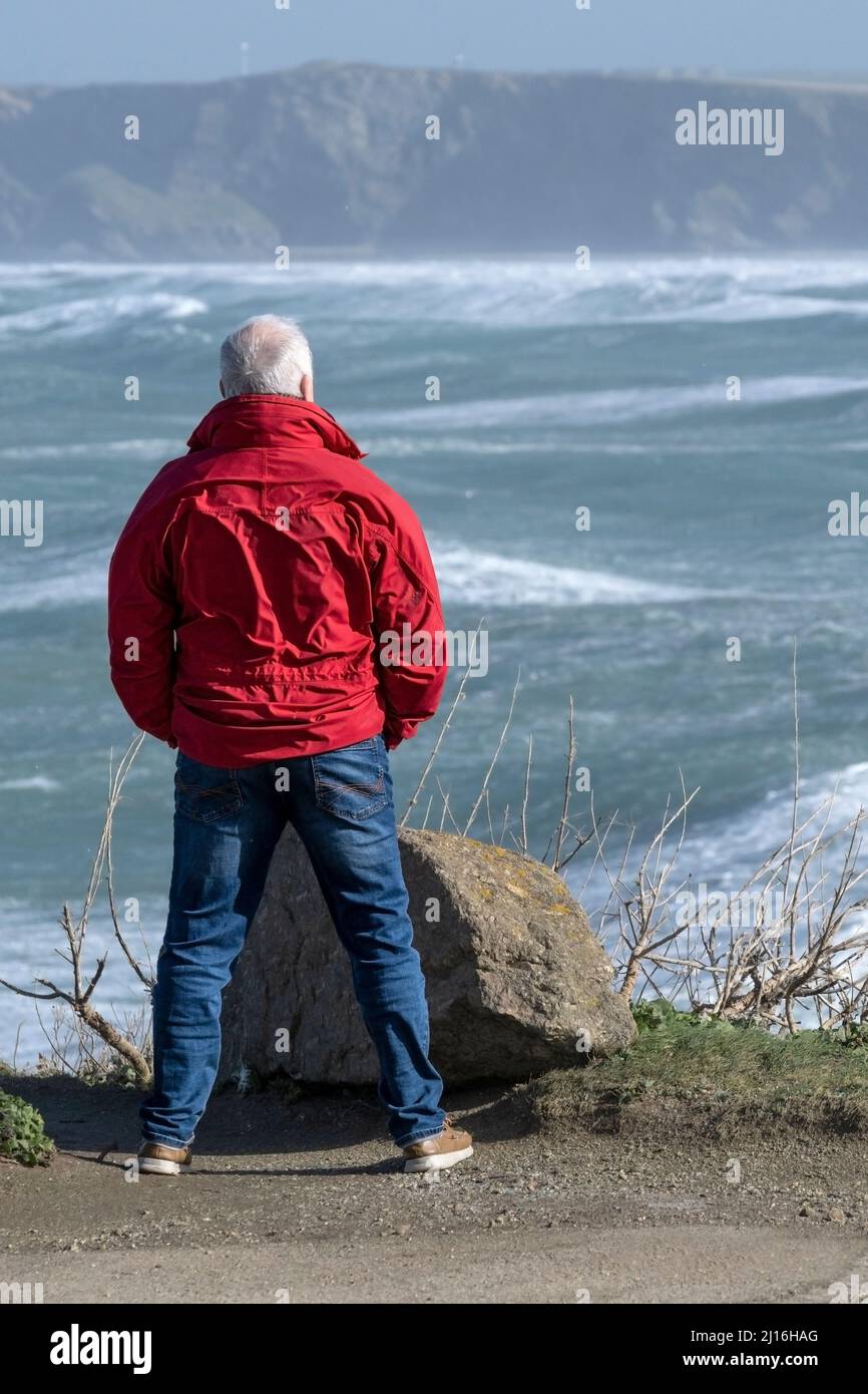 A man in a bright red jacket standing braced against the storm force ...