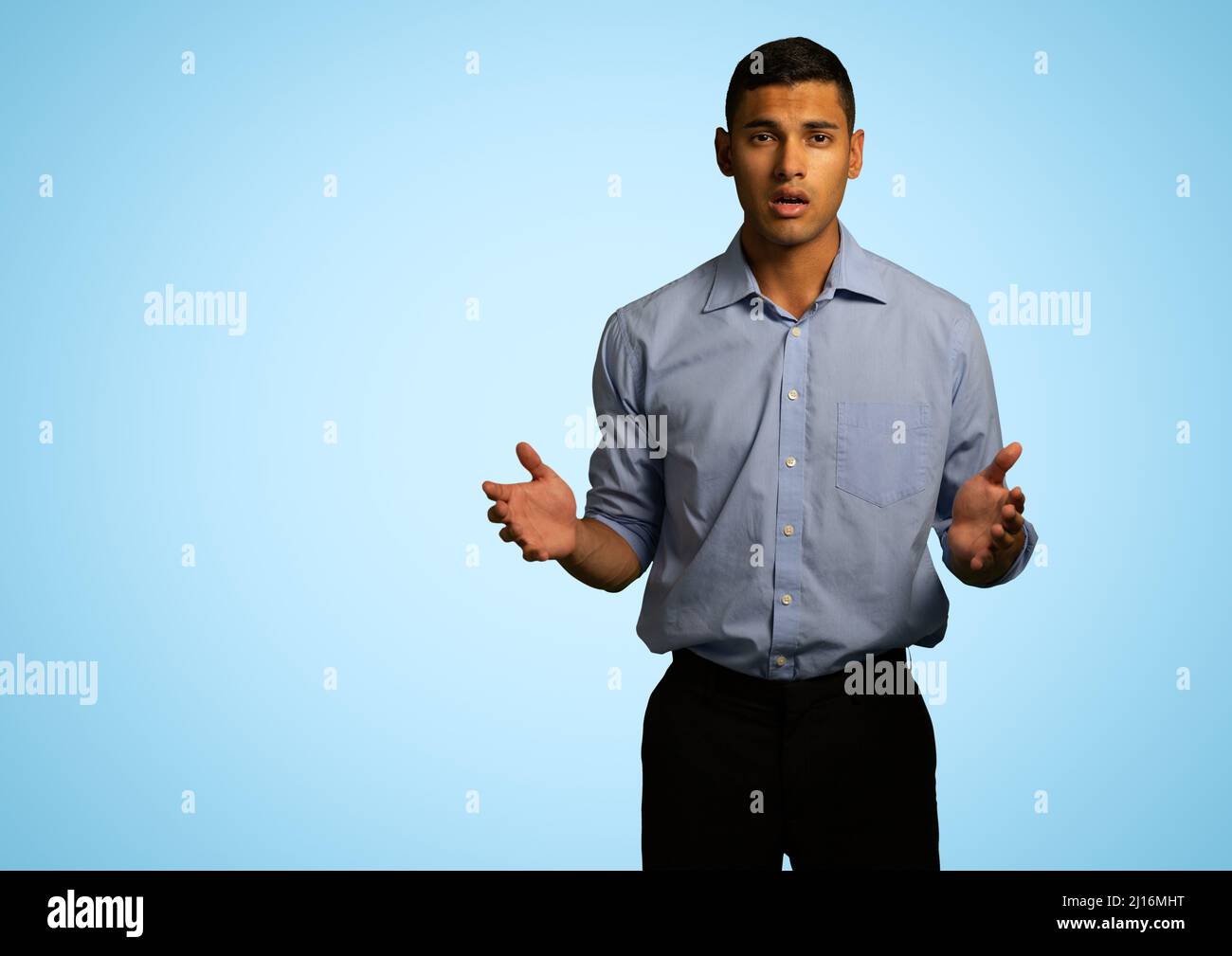 Confused indian man with his hands sideways against copy space on blue ...