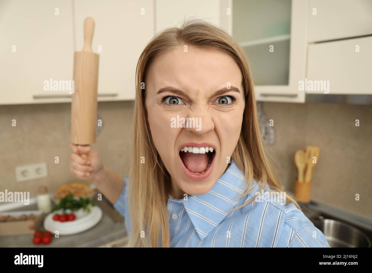 Angry young woman with rolling pin in kitchen room Stock Photo - Alamy