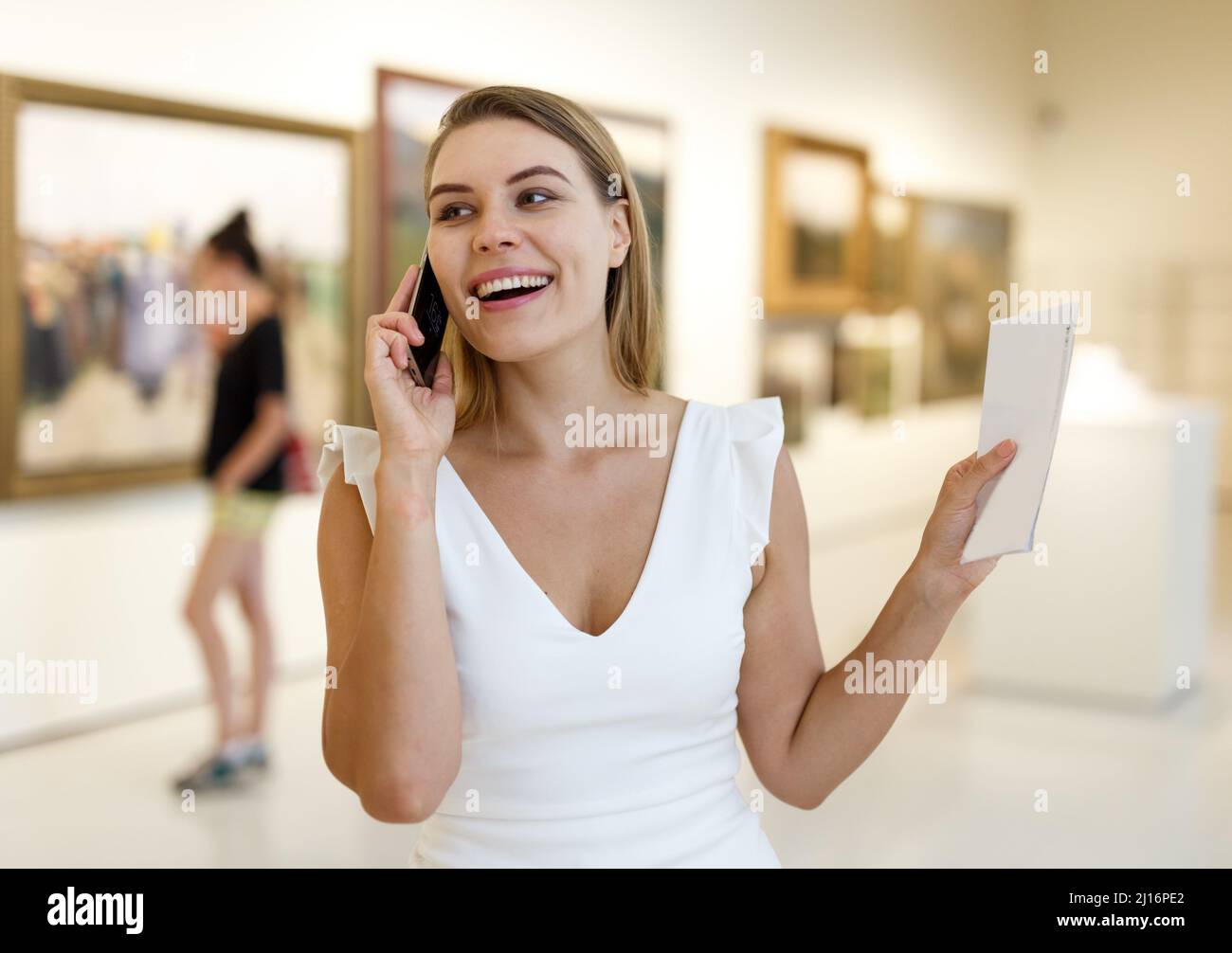 Smiling woman talking by mobile phone during visit at art gallery Stock ...
