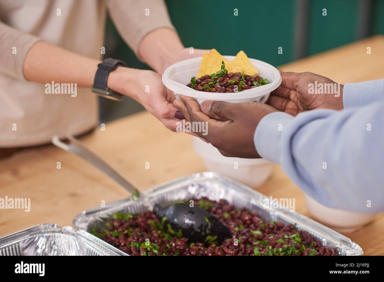 Medium close-up shot of unrecognizable volunteer giving plate with meal to beneficiaries in ...
