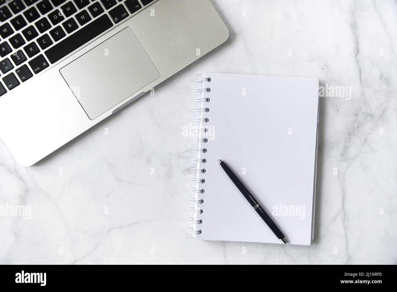 Overhead of laptop computer and notebook on white marble background ...