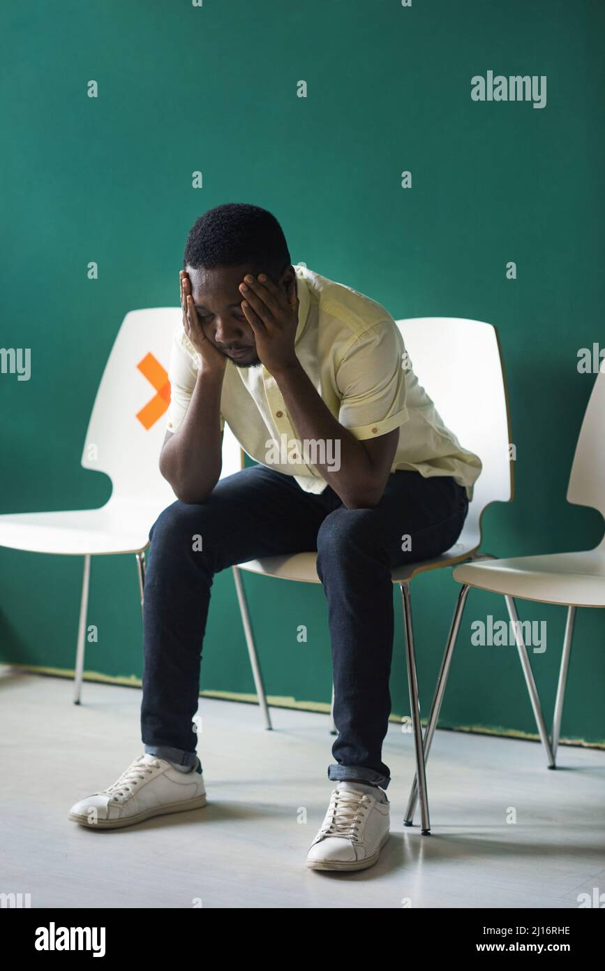 Vertical full shot shot of African American young man sitting alone on ...