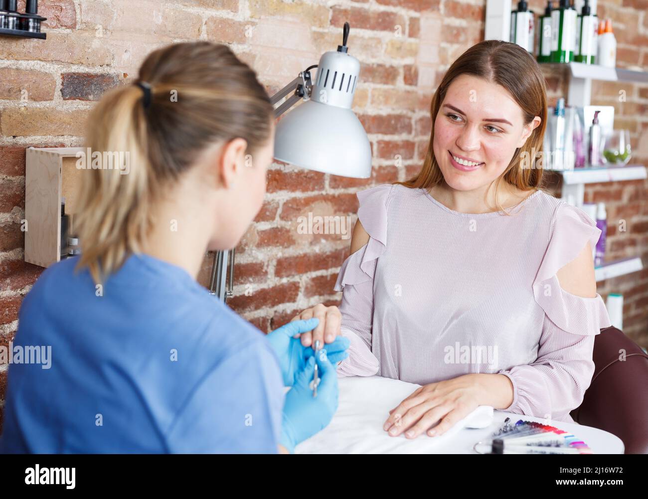 Professional manicurist doing manicure by nail to girl in modern beauty ...