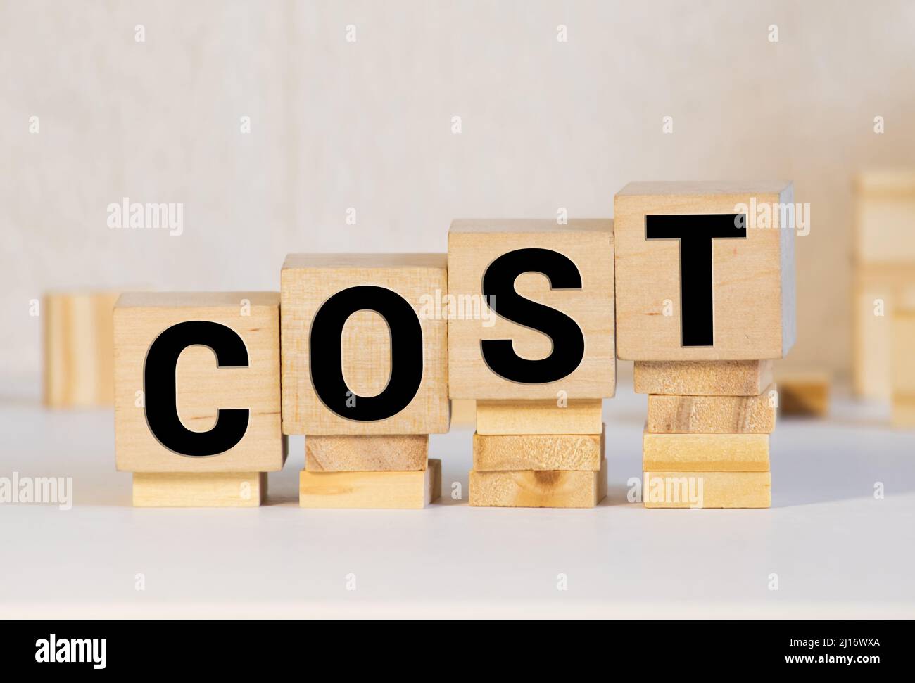 COST word written on wooden blocks on stacks of coins with grey ...