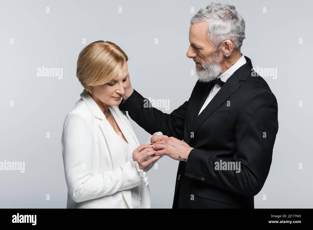 Mature groom touching bride with wedding ring isolated on grey Stock ...