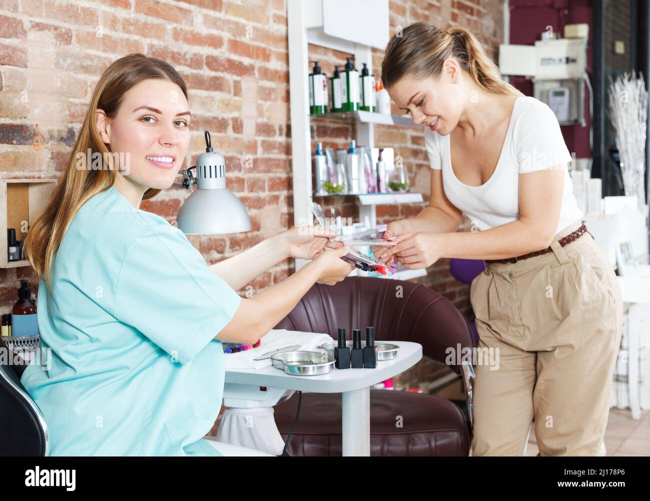 young client choosing color of nail polish, talking with manicurist ...