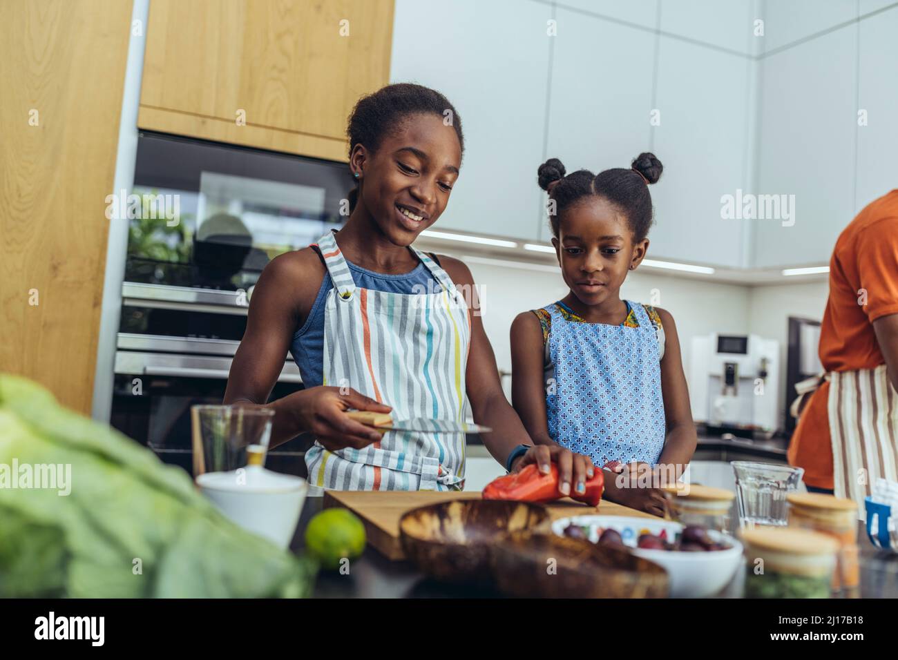 Girl cutting vegetables by sister in kitchen Stock Photo - Alamy