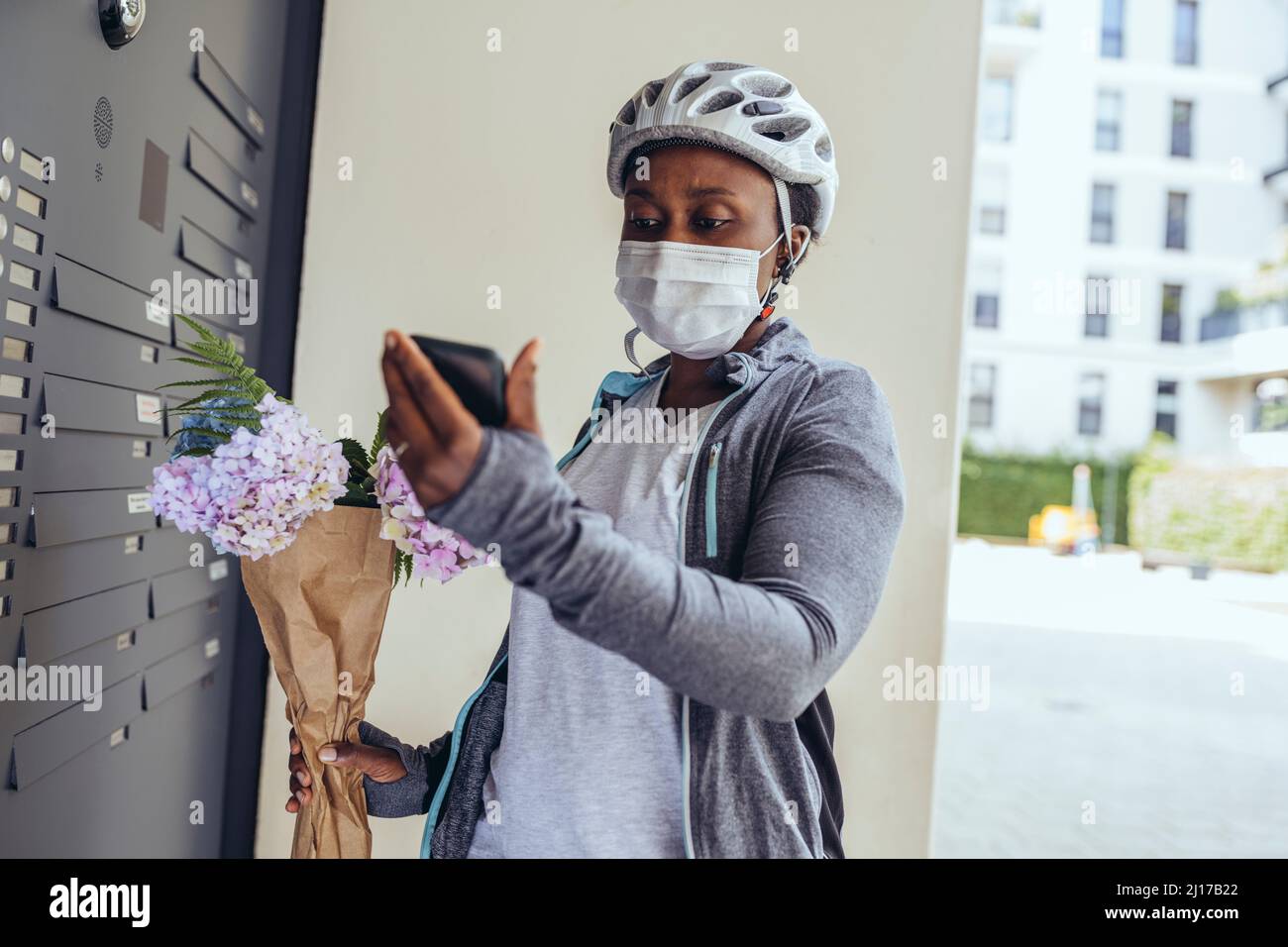 Delivery woman with protective face mask holding bouquet at entrance ...
