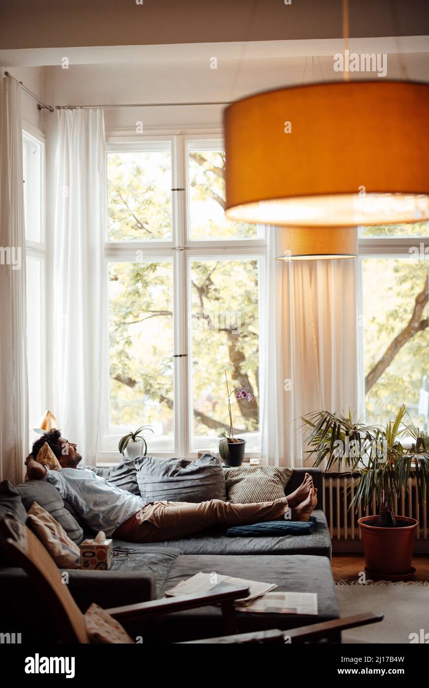 Man lying on sofa in living room at home Stock Photo - Alamy