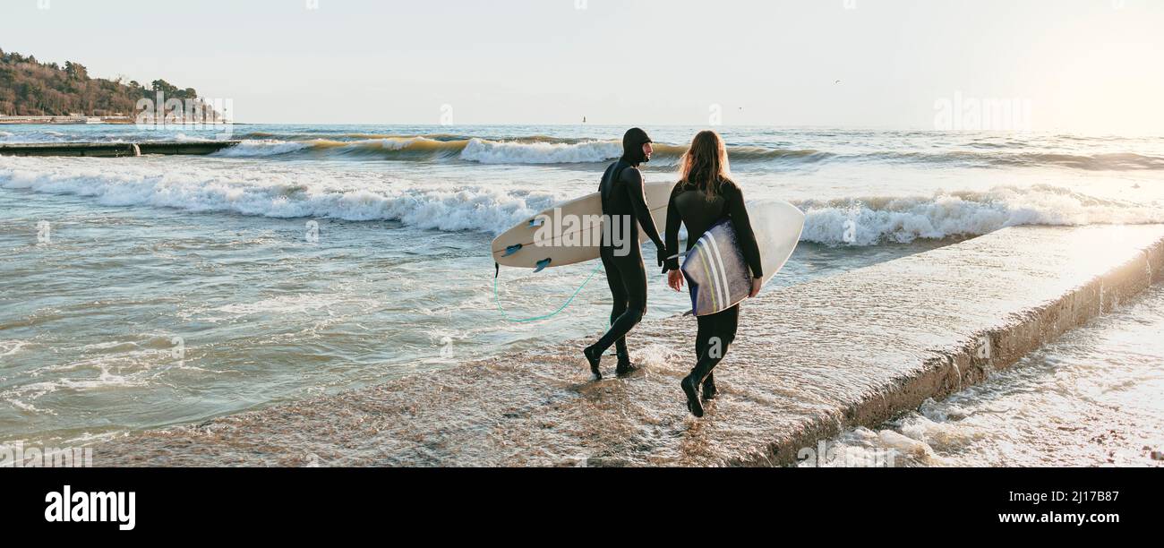 Surfers walking on concrete jetty with surfboard Stock Photo - Alamy
