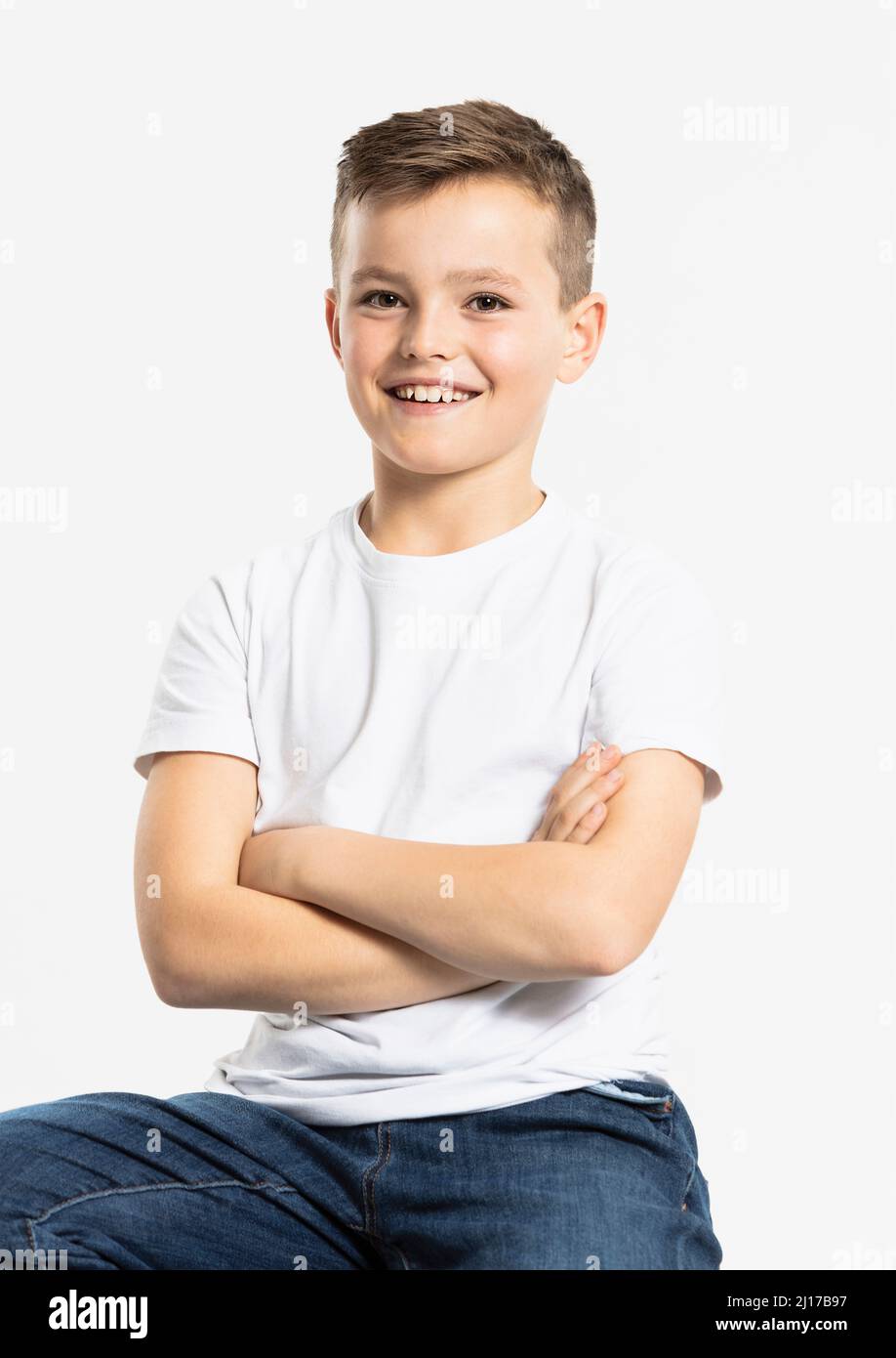Happy boy sitting with arms crossed at studio Stock Photo - Alamy