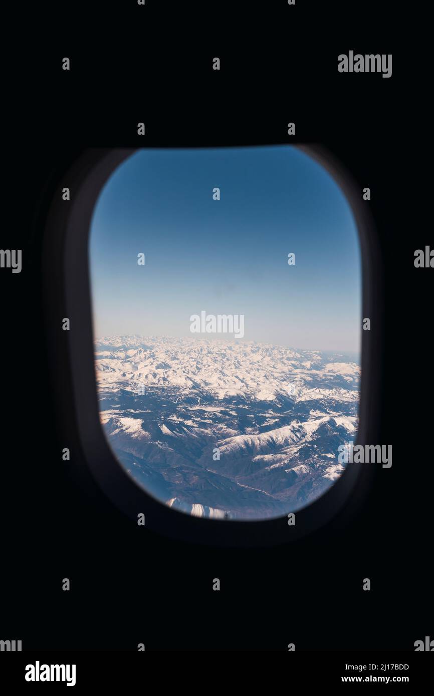 Snow covered mountains seen through airplane window Stock Photo - Alamy