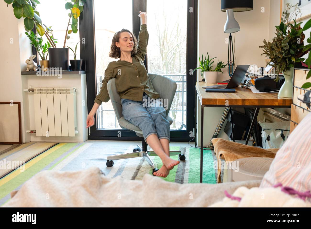 Tired young woman with hand raised sitting on chair at home Stock Photo ...