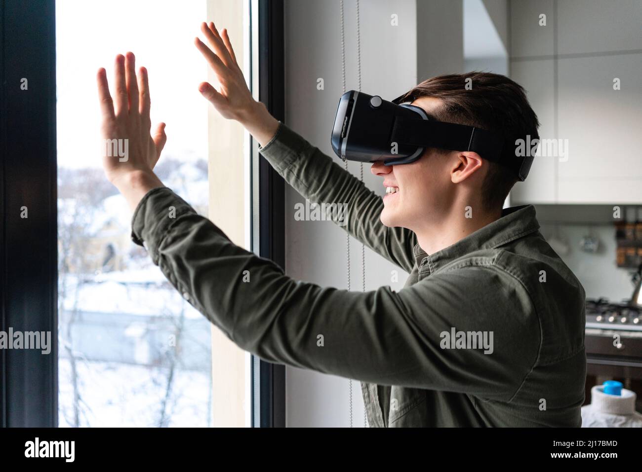 Smiling young man wearing virtual reality simulator touching glass ...