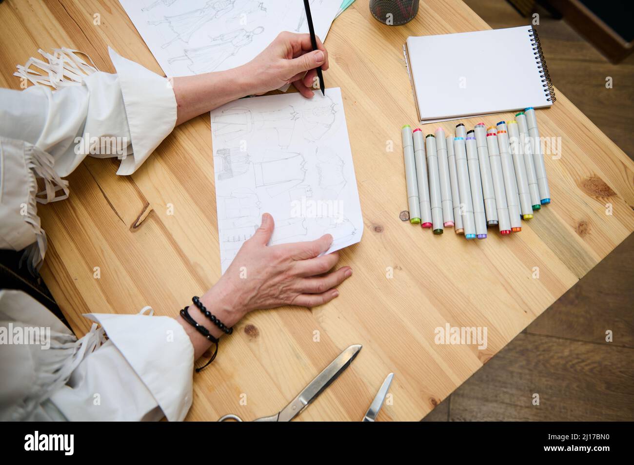 Overhead view of a female fashion designer, dressmaker drawing sketches ...