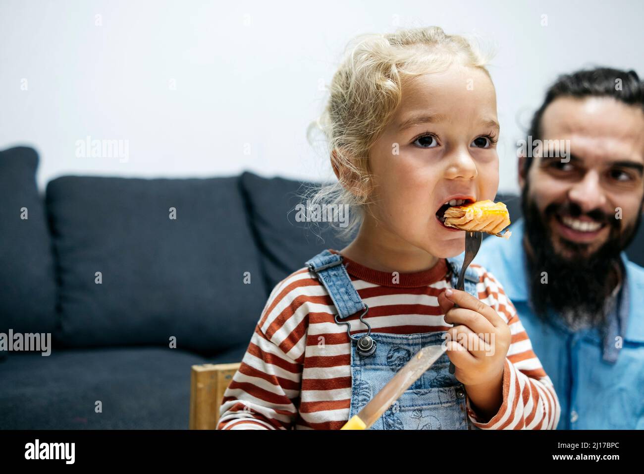 Blond boy eating food by father at home Stock Photo - Alamy