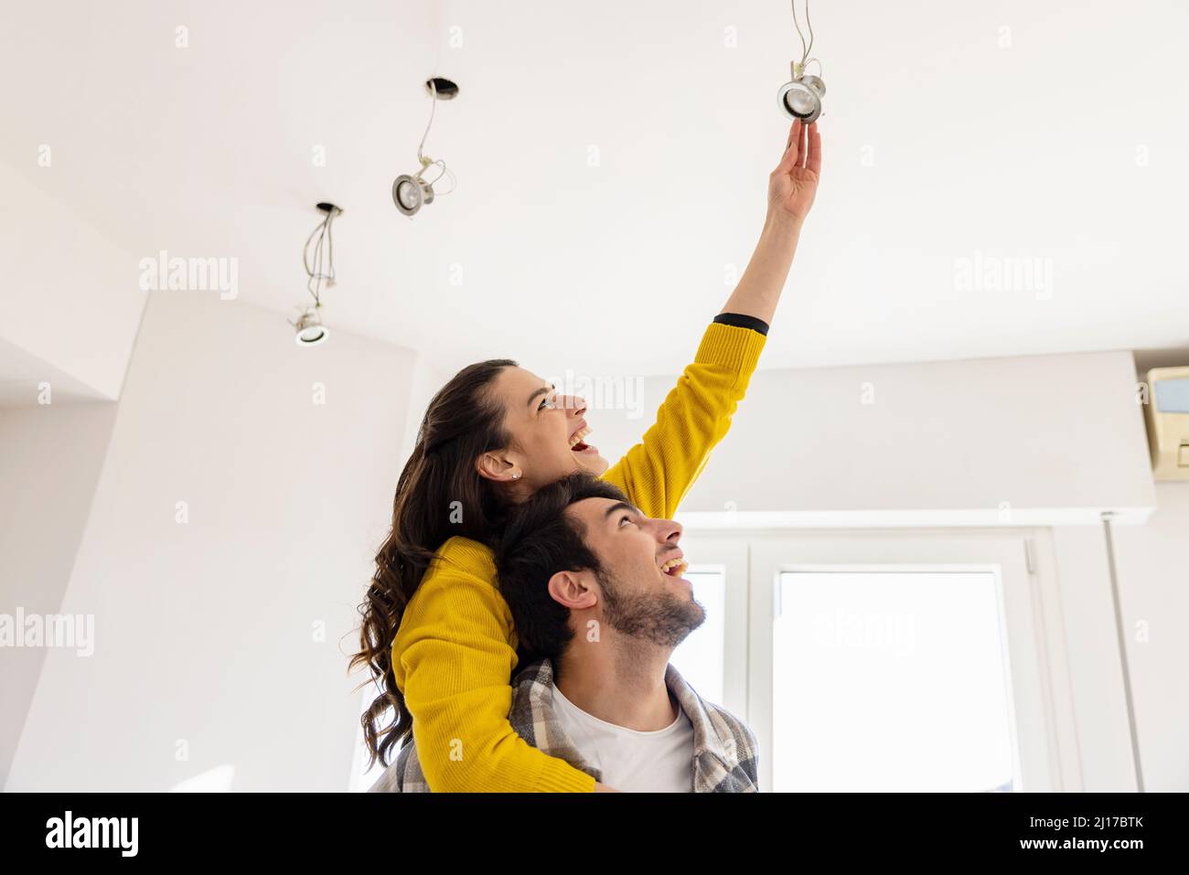 Happy woman changing light bulb on boyfriend's back at new home Stock ...