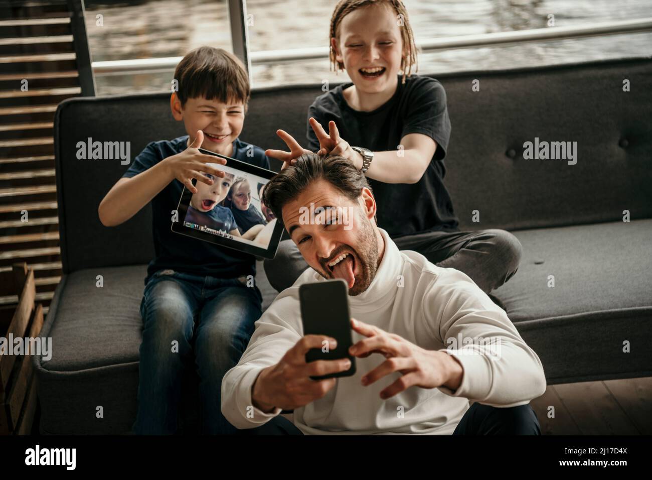 Playful man with sons taking selfie through smart phone at home Stock ...