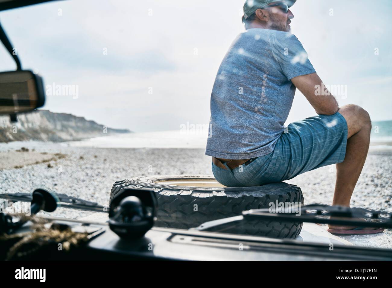 Man sitting on tire seen through windshield of car Stock Photo - Alamy