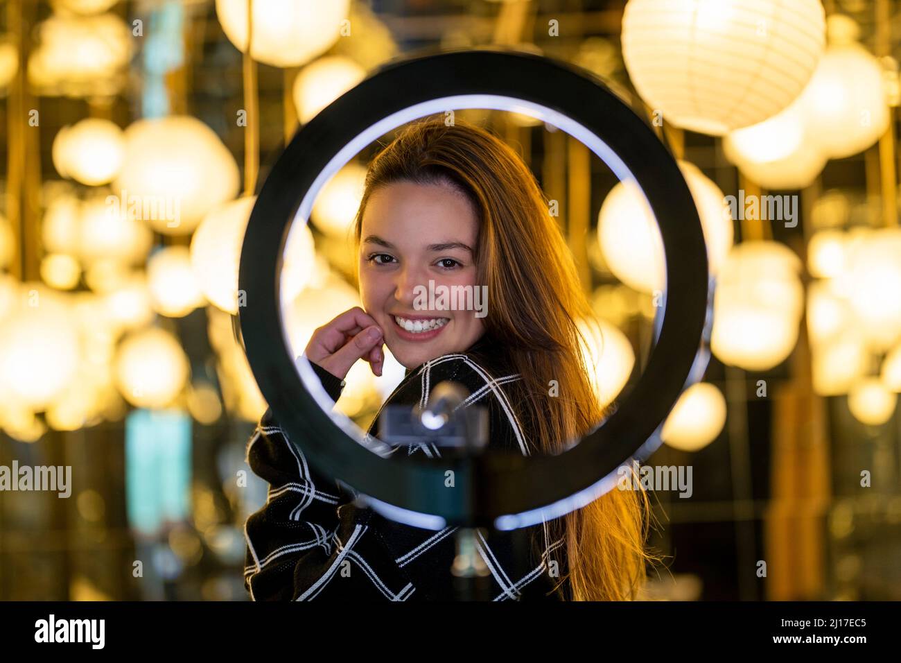 Happy woman smiling through ring light in front of lanterns Stock Photo ...