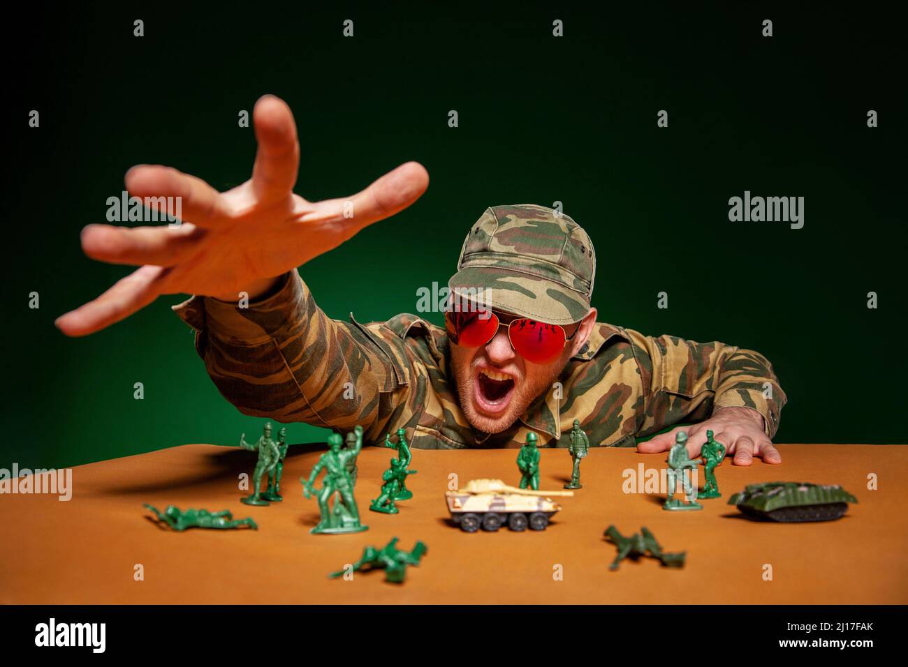Military soldier in uniform screaming and reaching figurines on table ...