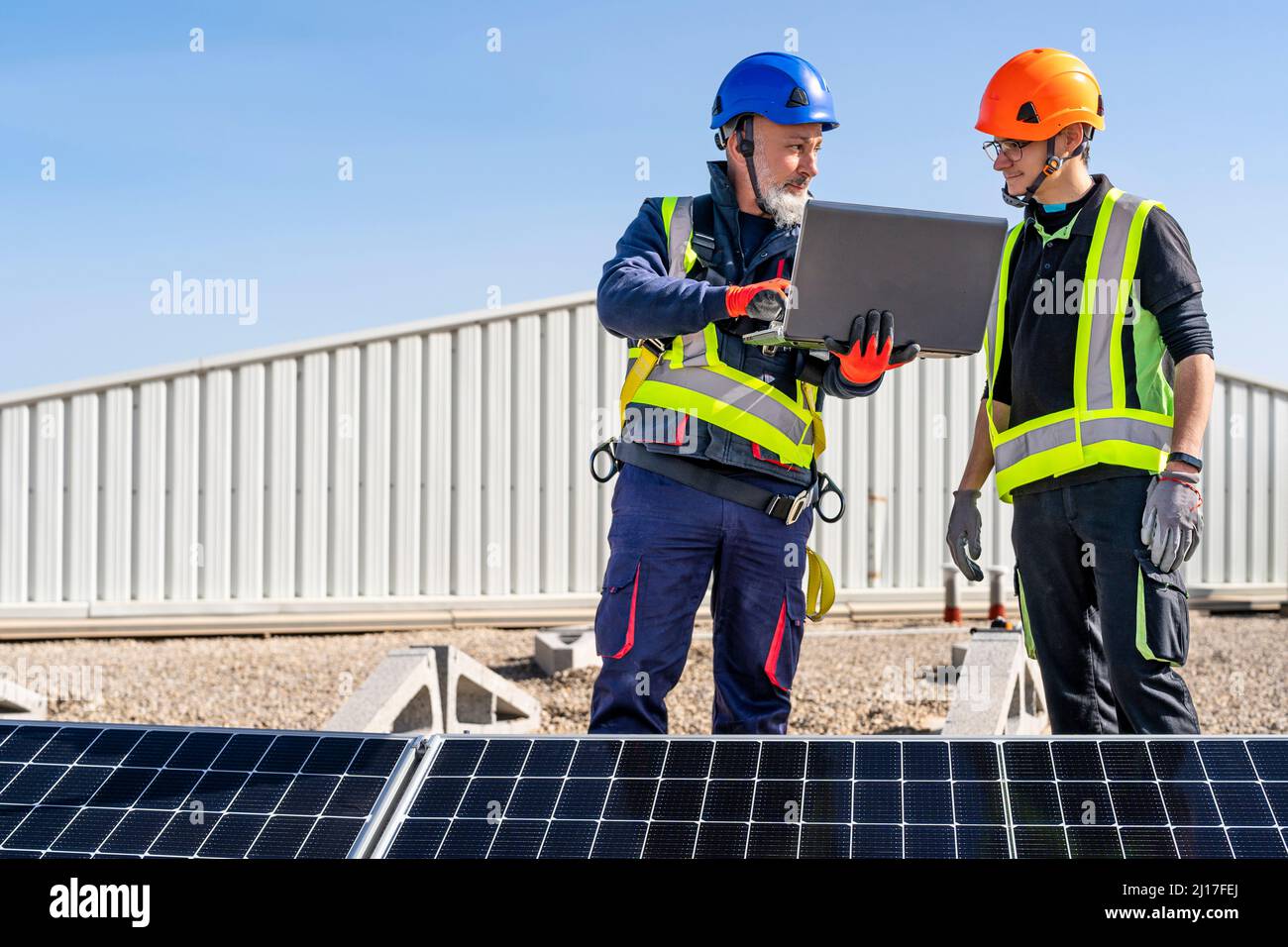 Technician with laptop discussing with colleague at solar power station ...