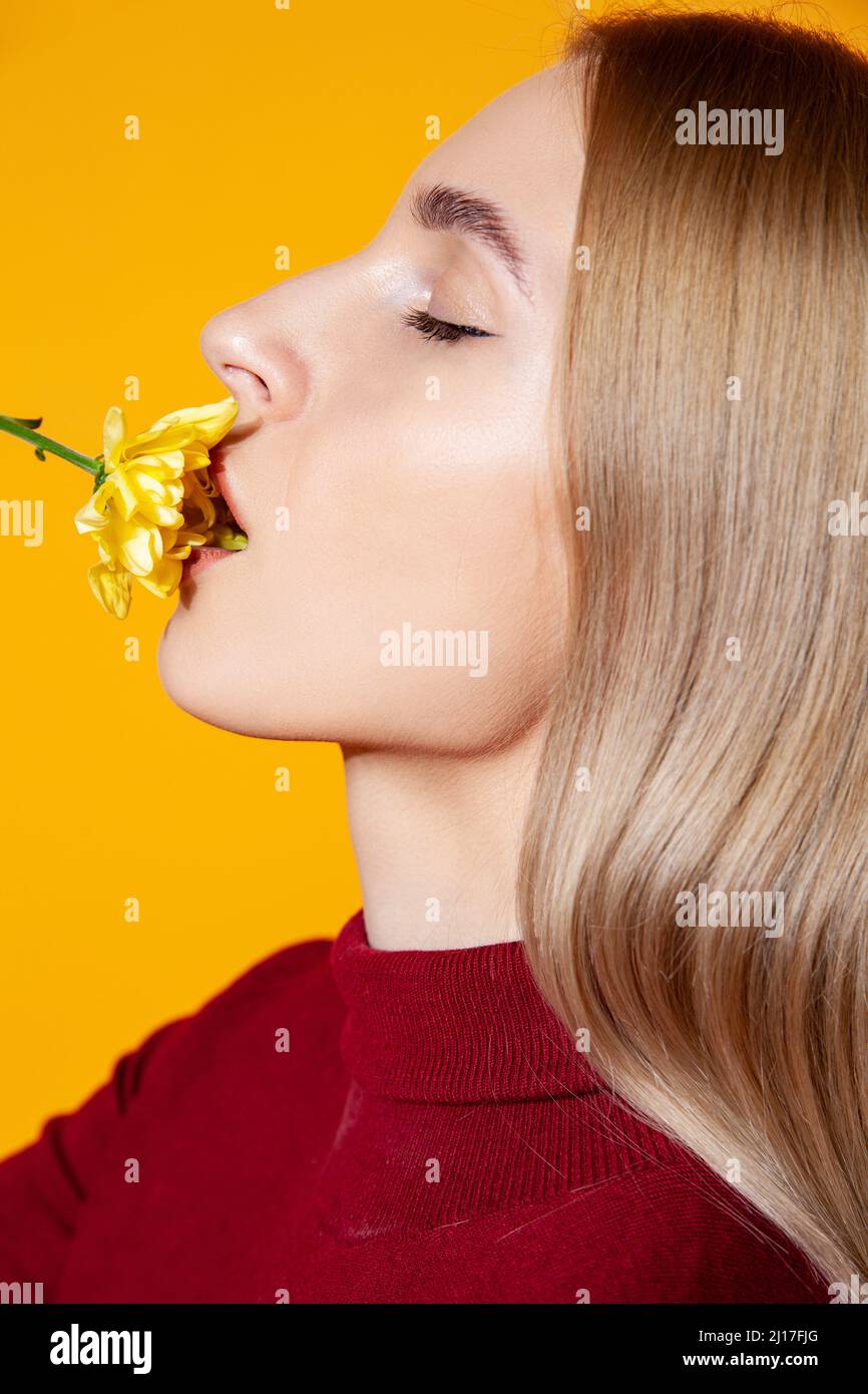 Blond woman eating flower by yellow background Stock Photo - Alamy