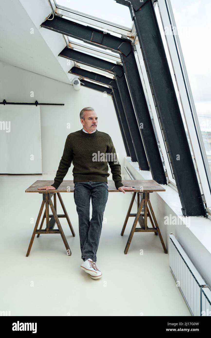 Thoughtful businessman looking out of window at work place Stock Photo ...