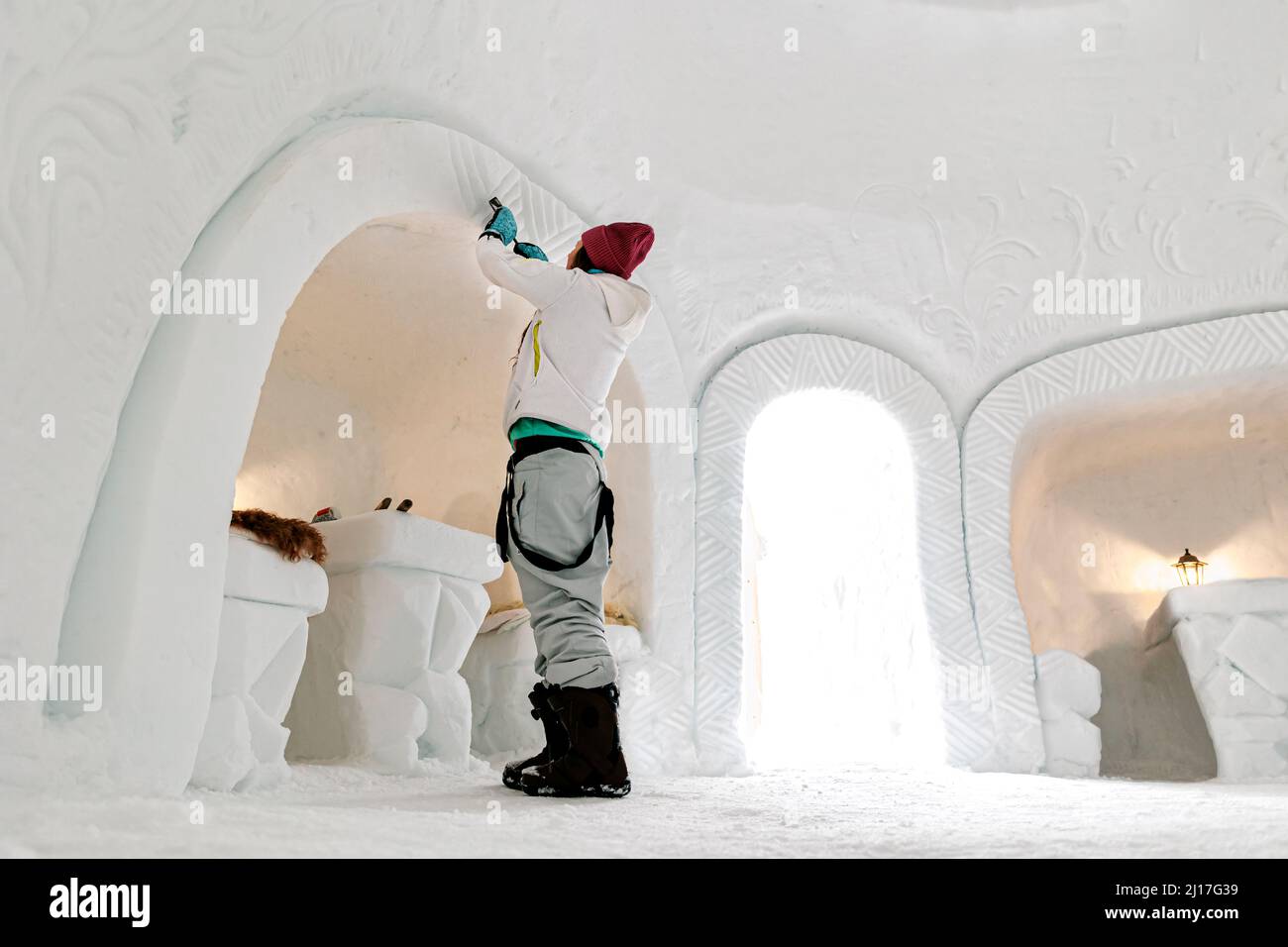 Woman with warm clothing and knit hat carving snow in igloo Stock Photo ...