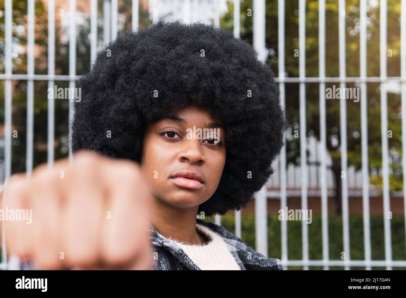 Confident woman showing fist in front of fence Stock Photo - Alamy
