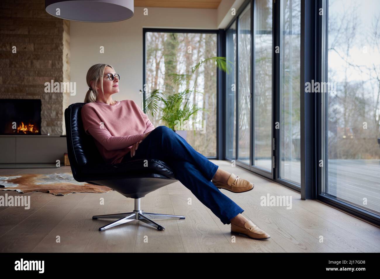 Woman looking through glass window sitting on chair in living room ...