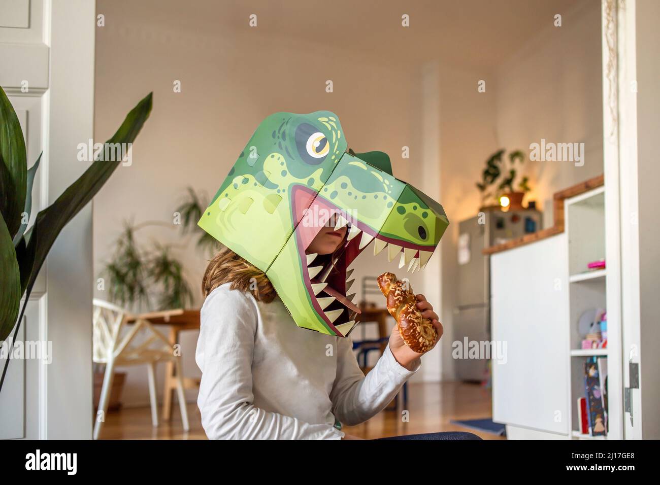 Girl with Dinosaur mask having bread at home Stock Photo - Alamy