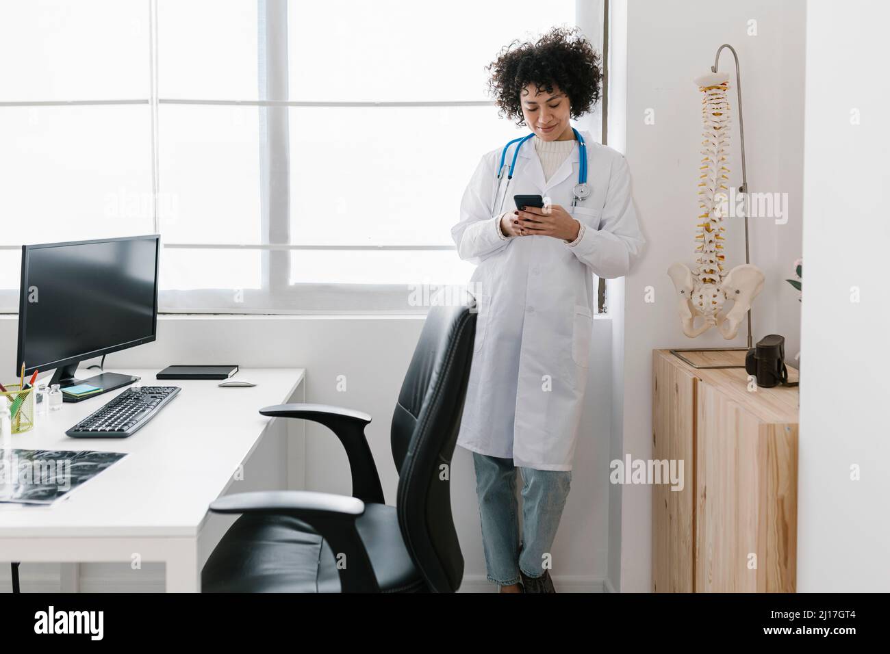 Smiling doctor using smart phone by window in medical office Stock ...