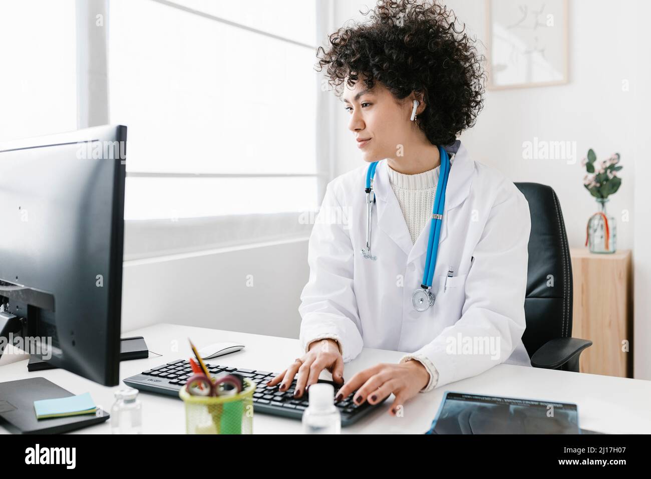 Doctor wearing in-ear headphones using desktop PC at medical clinic ...