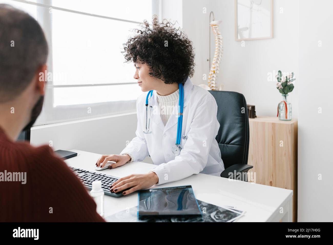 Young doctor using computer sitting with patient at medical clinic ...
