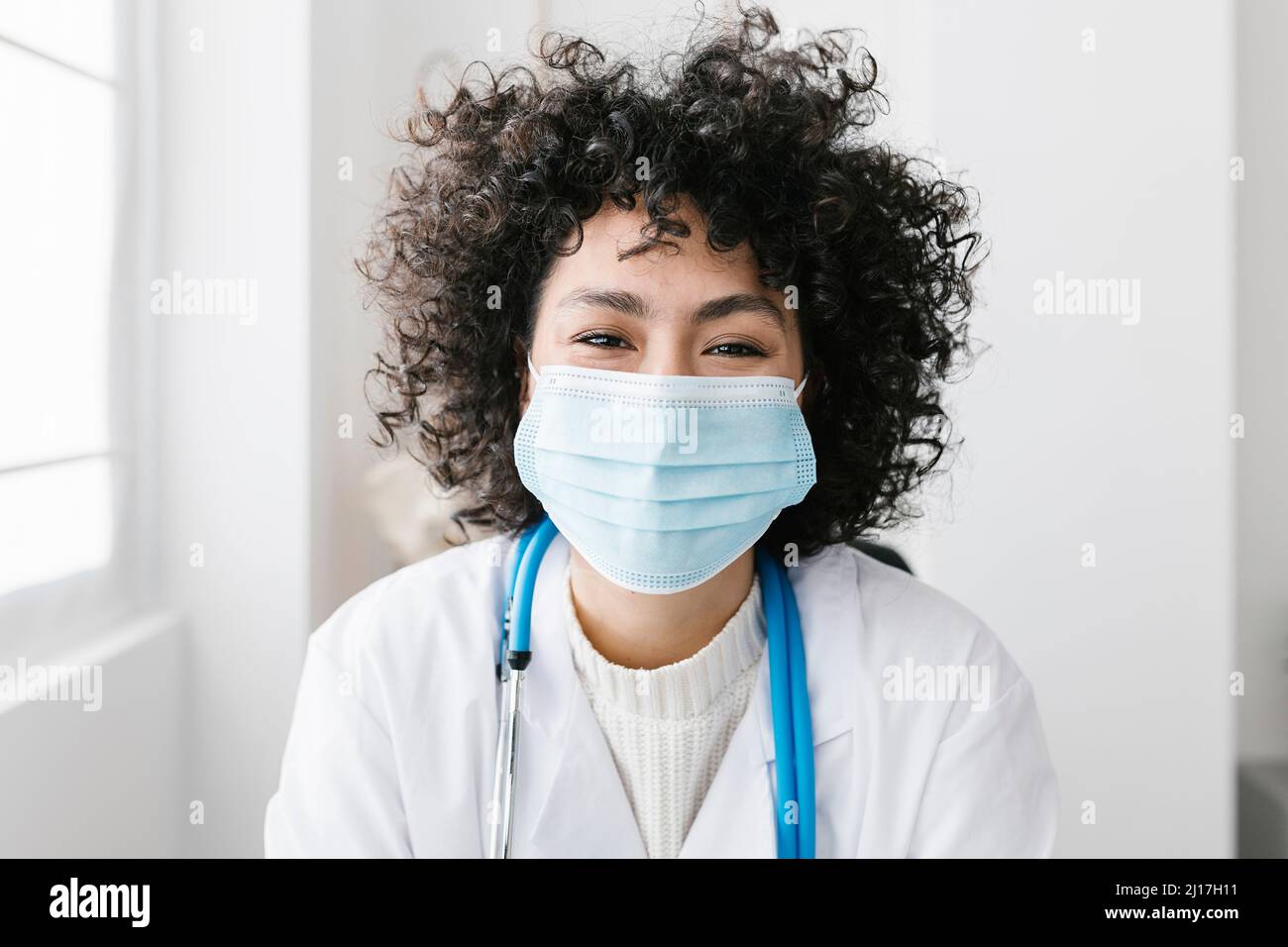 Young doctor with curly hair wearing protective face mask in medical ...