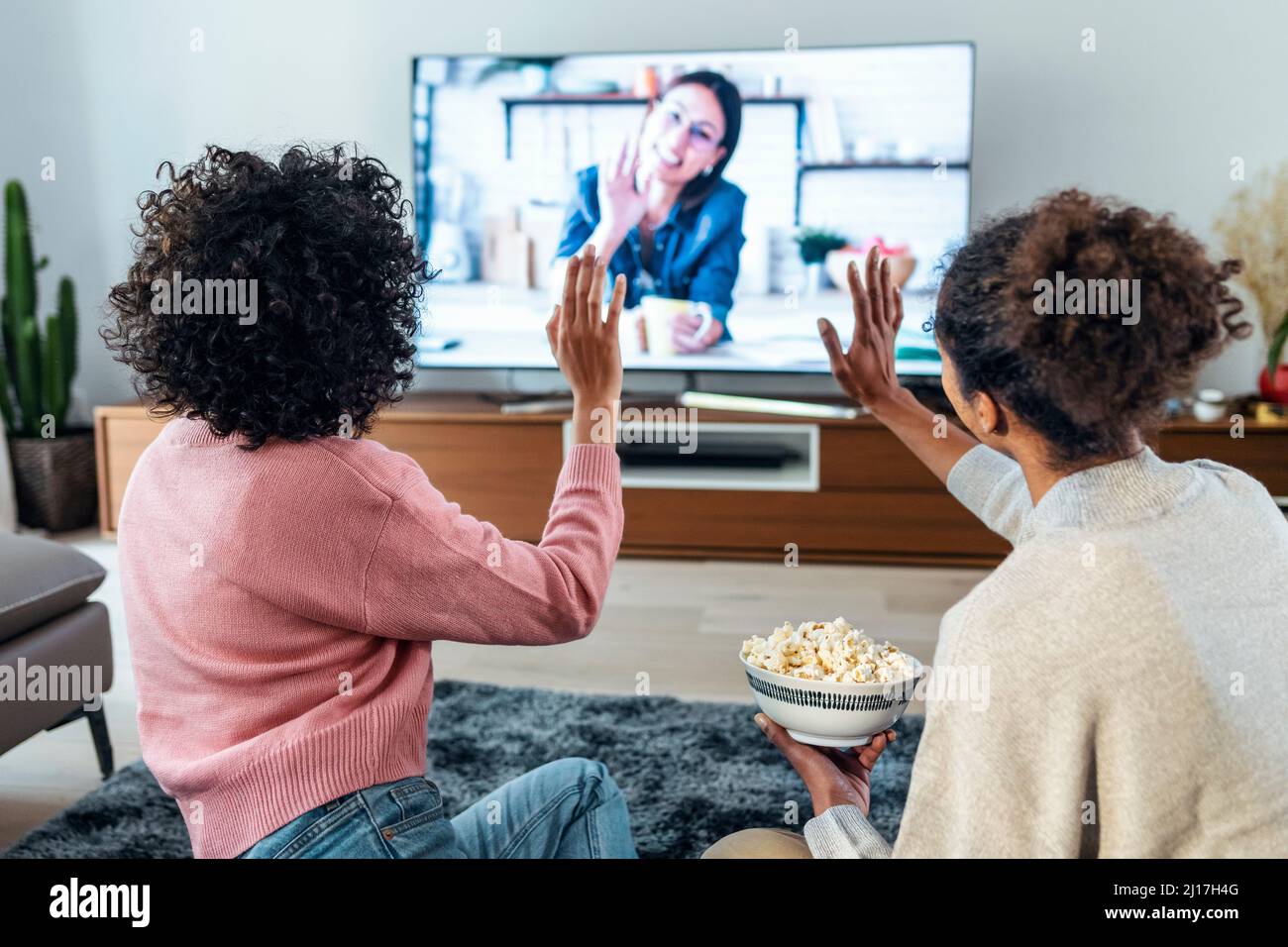 Women waving hands on video call with friend through television set at ...